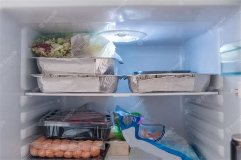 Открытый холодильник со светом, наполненный сырыми овощами и фольгой ...