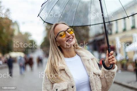 투명한 우산을 쓴 노란 선글라스를 쓴 귀여운 웃는 금발 여자가 도시 거리를 따라 걷는다 생활방식 비에 대한 스톡 사진 및 기타 이미지 Istock