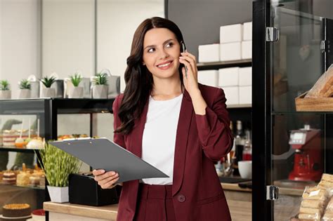 그녀의 카페에 있는 사업주 클립보드를 들고 패스트리를 들고 쇼케이스 근처에서 전화 통화를 하는 여자 25 29세에 대한 스톡 사진 및 기타 이미지 Istock