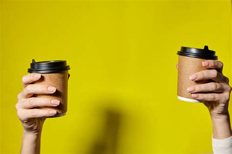 검은 색 뚜껑이있는 두 컵 갈색 종이를 들고 있는 손 2 개의 커피 특별 제안 또는 프로모션 노란색 화면 배경에 두 개의 컵을 들고 있는 손 차 나 커피 갈 수 있습니다
