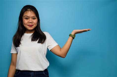 손바닥에 파란색으로 격리된 배경 복사 공간이 있는 흰색 티셔츠를 사용하는 아름다운 아시아 여성 프리미엄 사진