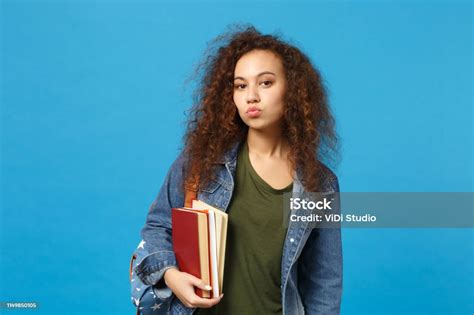 데님 옷에 젊은 아프리카계 미국인 소녀 사춘기 학생 배낭은 파란색 벽 배경 스튜디오 초상화에 고립 된 책을 잡아 고등학교 대학 대학 개념에서 교육 복사 공간을 모의 가방에