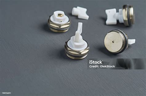 작업장에서 어두운 긁힌 책상에 방에 히터 라디에이터에서 과도한 공기와 압력을 배출하기 위한 흰색 플라스틱 손잡이가 있는 흩어진 금속 공기 밸브의 많은 텍스트를 위한 공간