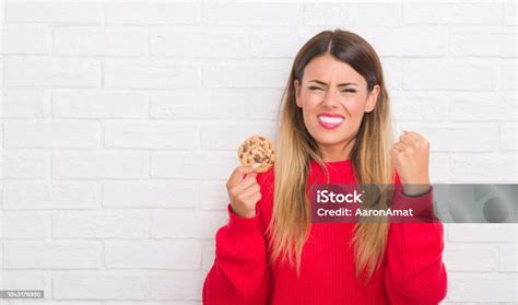 흰색 벽돌 위에 젊은 성인 여자 벽 화가 초콜릿 칩 쿠키 먹고 미친과 제기 손으로 소리 분노와 좌절 외치고 분노 개념 갈색 머리에 대한 스톡 사진 및 기타 이미지 Istock