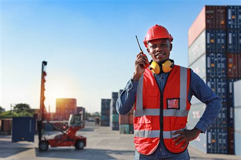 워키토키 무선 제어 적재 컨테이너 상자를 사용하는 감독 엔지니어 컨테이너 화물 현장에서 헬멧 작업을 통한 자신감 있는 엔지니어링 및 산업용 컨테이너 화물 운송 선박 점검