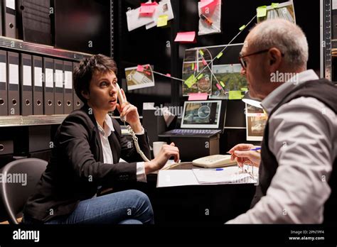 private detective discussing with remote inspector at landline phone working late at night at