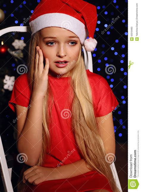 Фото рождества милой маленькой белокурой девушки в шляпе Santa и красном платье Стоковое