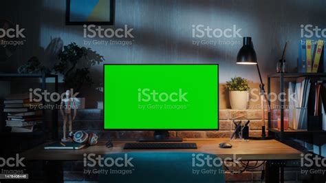 높이 조절 기능이있는 나무 책상에 서있는 모의 그린 스크린이있는 데스크탑 컴퓨터 모니터 현대 거실 또는 벽돌 벽이있는 크리에이티브 로프트 사무실에서 집에서 크로마 키