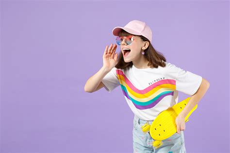 생생한 옷에 쾌활 한 십 대 소녀 안경은 옆으로 찾고 보라색 배경에 고립 된 손 제스처와 비명 스케이트 보드를 개최 합니다 사람들은 진심으로 감정 라이프 스타일 개념입니다