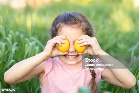 눈과 웃음 대신 노란 부활절 달걀을 들고 푸른 잔디의 배경에서 재미를 느끼는 귀여운 소녀 아이들은 행복한 부활절을 축하합니다 놀라움에 대한 스톡 사진 및 기타 이미지