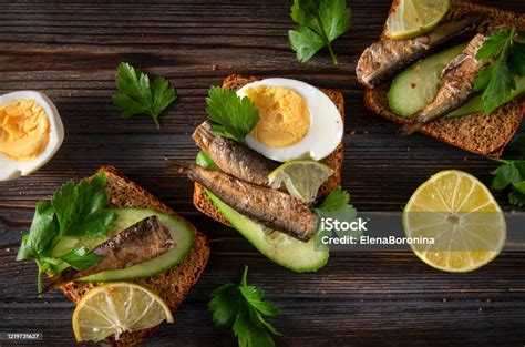 스프래트 파슬리 라임 신선한 오이 호밀 빵 삶은 달걀을 곁들인 샌드위치 3개 어두운 나무 배경 꼭대기 전망 통조림 생선 끓는 물에 삶기에 대한 스톡 사진 및 기타 이미지