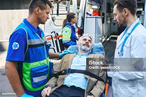 구급차 거니에 누워있는 노인 남성 환자를 검사하는 구급 대원 및 의사는 Emt 근로자가 병원에 데려왔다 응급 의료 서비스 및 사람에 대한 배려 부상에 대한 스톡 사진 및