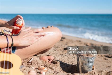 알아볼 수 없는 성인 백인 여성이 맨발로 바다 해변의 모래 위에서 섹시한 다리에 자외선 차단제를 바르고 여름철 피부 자외선 차단을 위해 30 39세에 대한 스톡 사진 및