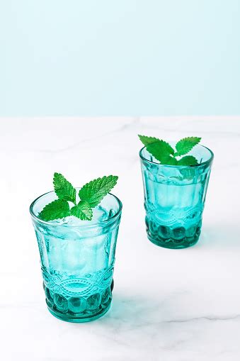 차가운 음료와 얼음 조각이있는 두 개의 아름다운 빈티지 청록색 안경 흰색 대리석 테이블에 신선한 녹색 민트 잎으로 장식 0명에
