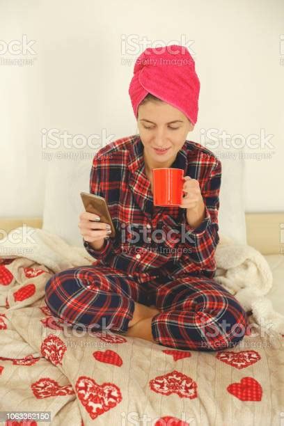 스마트폰으로 인터넷을 서핑 하 고 침대에 누워 수건에 싸여 젖은 머리를 가진 아름 다운 소녀 Brand Name Online Messaging Platform에 대한 스톡