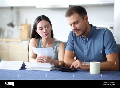 Interracial Couple Calculating Expenses Reading Bill In The Kitchen At Interracial Couple Calculating Expenses Reading Bill In The Kitchen At