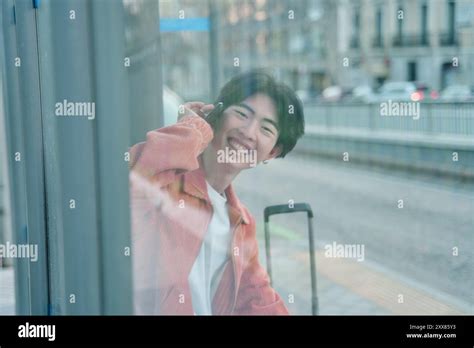 Attractive Young Asian Man Talking On The Phone While Waiting For The Bus Looking At The Camera