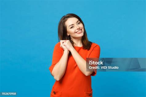 아름 다운 꿈 같은 갈색 머리 젊은 여 자가 파란색 벽 배경 스튜디오 초상화에 고립 된 포즈 서 있는 소원을 만드는 빨간 오렌지