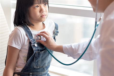 백색 제복 가운에 있는 직업적인 일반적인 의학 소아과 의사는 청진 기를 가진 아시아 아이 환자의 폐와 심 음을 경청 한다 의사는 병원에서 상담 후 아시아 아이 여자를 확인