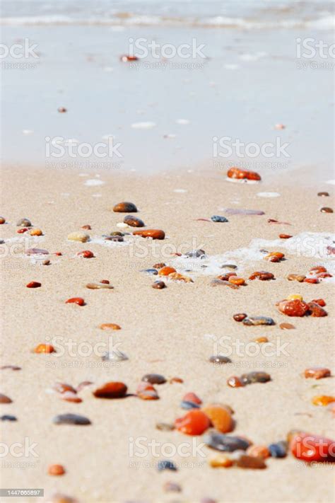 바다 돌은 천연 베이지색 모래 해안 배경에 주황색 노란색으로 표시되어 공간을 복사합니다 자연의 다채로운 자갈과 해변의 바다 파도 단색 톤 최소한의 자연 여름 풍경 여행