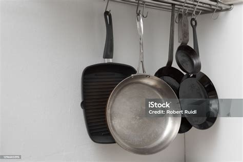 다양한 크기의 다양한 팬과 흰색 벽이있는 부엌선반의 금속 후크에 매달려 요리하고 튀기는 포식 프라이팬에 대한 스톡 사진 및 기타 이미지 Istock
