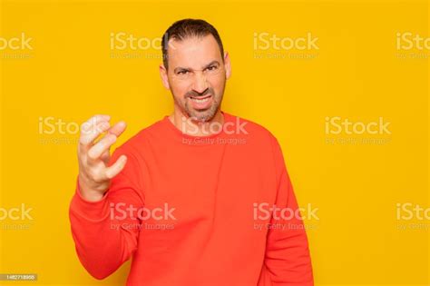 빨간 스웨터를 입은 중년의 수염 난 남자는 명백한 화나고 공격적이며 사려 깊은 표정으로 발톱을 몸짓으로 합니다 노란색 배경에 격리 35 39세에 대한 스톡 사진 및 기타