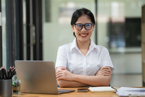 매력적인 젊은 아시아 사업가 또는 여성 사무실 직원이 안경을 쓰고 사무실 책상에 앉아 웃으며 카메라를 바라보고 있다 경영자에 대한 스톡 사진 및 기타 이미지 Istock