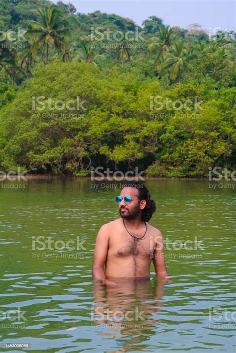 착색된 거울 선글라스를 쓴 인도 남자의 이미지는 석호 열대 섬 낙원 야자수가 있는 삼림 지대의 전망 전경에 초점을 맞춘 잔잔한 물에 허리 깊숙이 서 있었습니다 30 34세에