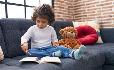Adorable Hispanic Girl Drawing On Notebook Sitting On Sofa At Home