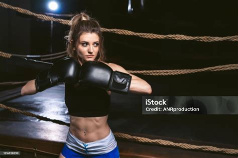 스포츠웨어의 어린 소녀 권투 장갑을 착용 티셔츠와 반바지 어두운 체육관에서 복싱 링의 배경에 포즈를 취하는 운동 여자 힘과 동기
