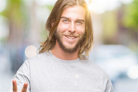 격리 된 배경에 보여주는 손가락 승리 표시를 하 고 카메라를 보고 웃 긴 머리를 가진 젊은 잘생긴 남자 번호 2입니다 긍정적인 감정 표현에 대한 스톡 사진 및 기타 이미지