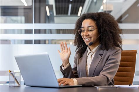 아프리카계 미국인 젊은 사업가가 사무실의 테이블에 앉아 노트북 화면을 통해 화상 통화로 대화하고 카메라를 향해 미소를 지으며 손을 흔드는 모습 거리가 먼에 대한 스톡 사진