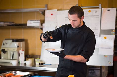 테마 요리는 요리의 직업입니다 검은 장갑 유니폼에 붉은 물고기 필렛 연어 고기를 준비 하는 레스토랑 부엌에서 백인 남자의 초상화 요리사는 파란색과 체크 취향에 접시를 보유