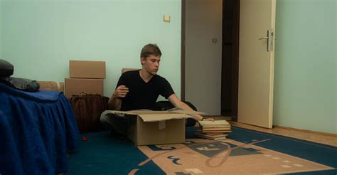 기숙사에 있는 자신의 방으로 이사한 한 학생이 물건을 들고 골판지 상자를 들고 앉아서 서있는 동안 방에 배치하는 사진을 스톡합니다 20 24세에 대한 스톡 사진 및 기타