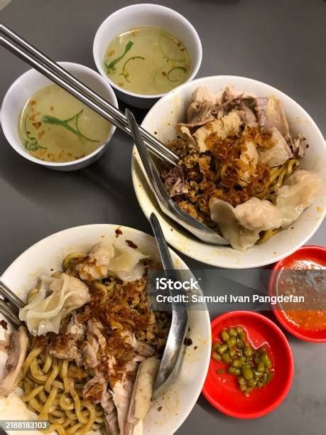 잘게 썬 닭고기 다진 고기 완탕 튀긴 샬롯을 얹은 풍미 가득한 국수 요리 두 그릇이 투명한 수프 그릇과 함께 제공됩니다 작은 빨간 접시에는 매운 양념이 담겨 있어 테이블에