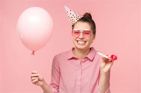 유색 안경과 생일 모자를 쓴 어린 행복한 소녀 휘파람 불기 분홍색 풍선 들고 웃고 파티를 즐기고 분홍색 배경에 고립 되어 있습니다 파티에 대한 스톡 사진 및 기타 이미지