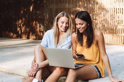 Dos Chicas J Venes Sonrientes Que Usan El Ordenador Port Til En El Parque Foto De Archivo