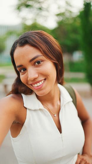 갈색 긴 머리를 가진 사랑스러운 소녀 흰색 상단을 착용 검게 그을린 피부는 휴대 전화를 사용하고 있습니다 핸드폰으로 셀카를 찍는 웃는 젊은 여성 감정에 대한 스톡 사진 및