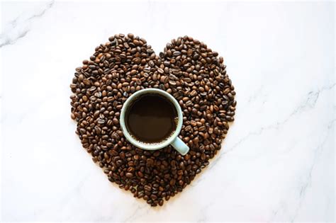 검은 커피로 가득 찬 중국 머그잔의 이미지 하트 모양의 구운 커피 콩 더미에 앉아 흰색 배경 높은 전망 복사 공간에 확산 0명에