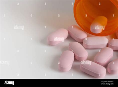 Oblong Pink Tablet Pills Spilt From A Medicine Bottle On A White