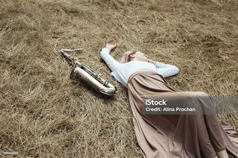 색소폰 옆에 마른 잔디에 누워 긴 드레스에 아름다운 젊은 여성의 몸 건초에 여름에 소녀는 악기 자연에 휴식의 개념과 함께 휴식 Theatrical Performance에