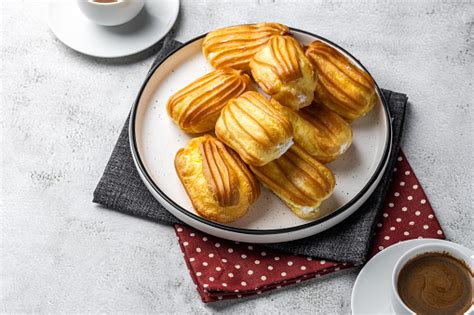 커스터드를 곁들인 프렌치 에클레어 흰색 접시에 크림을 곁들인 프로피테롤 상의 모습 크림을 곁들인 수제 패스트리 회색 배경입니다 커피를 곁들인 프로피테롤 0명에 대한 스톡