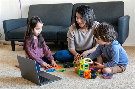 노트북을 들고 놀고 있는 아이들과 함께 거실에 앉아 있는 어머니 멀티 태스킹에 대한 스톡 사진 및 기타 이미지 멀티 태스킹 부모 3 명 Istock