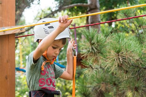 로프 파크 클라이밍 센터 보호 장비에서 걷기 어드벤처 파크에서 놀고있는 아기 소년은 장애물을 통과합니다 극단적 인 어린이의 레저 및 엔터테인먼트 스포츠는 민첩하고 대담한