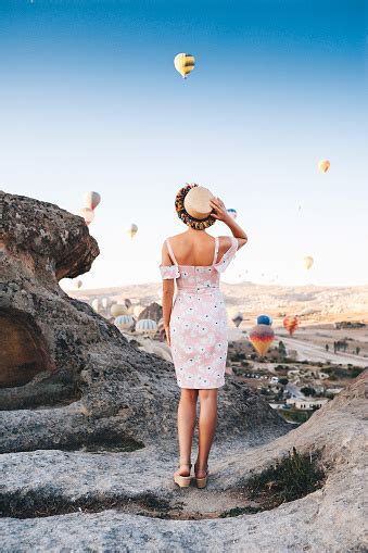 카파도키아의 일출과 풍선의 멋진 전망을 즐기는 산 꼭대기에 드레스와 모자를 쓴 젊은 여성 30 34세에 대한 스톡 사진 및 기타 이미지 30 34세 관광 관광객