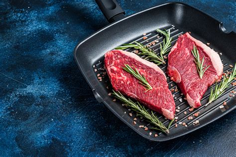 그릴 프라이팬에 생 엉덩이 또는 등심 쇠고기 고기 스테이크를 요리 할 준비가되었습니다 파란색 배경입니다 맨 위 보기입니다 복사 공간 0명에 대한 스톡 사진 및 기타 이미지