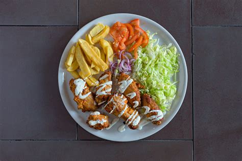 짙은 나무 테이블에 는 감자 튀김 녹색 샐러드 토마토를 곁들인 화이트 요거트 소스를 얹은 프라이드 치킨 윙의 세계 각국의 요리 0명에 대한 스톡 사진 및 기타 이미지