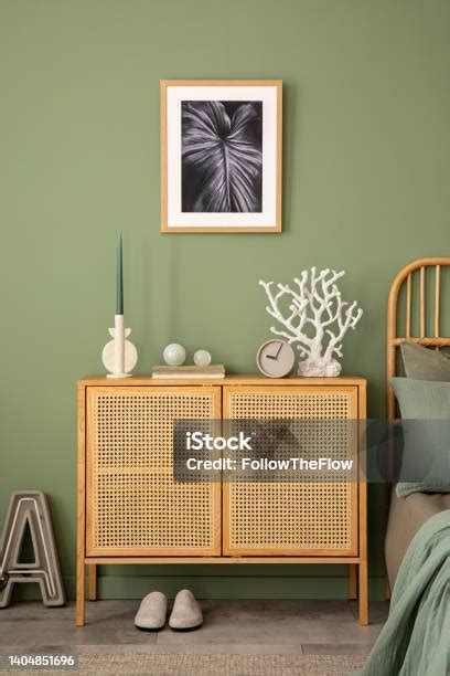 현대적인 침실 인테리어의 세련된 구성 포스터 프레임 등나무 Commode 아름다운 침구 및 창조적 인 개인 액세서리를 모의하십시오 녹색 벽 템플렛 공간을 복사합니다 침실에