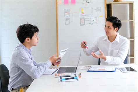 두 명의 아시아 남성이 휴대 전화에서 웹 사이트와 응용 프로그램을 디자인하기 위해 함께 일하고 있습니다 사진