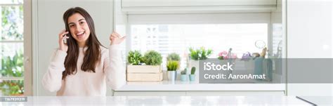 스마트 폰에서 대화를 하고 행복한 얼굴미소를 지으며 엄지 손가락으로 옆으로 보여주는 아름다운 젊은 여성의 광각 사진 가리키기에